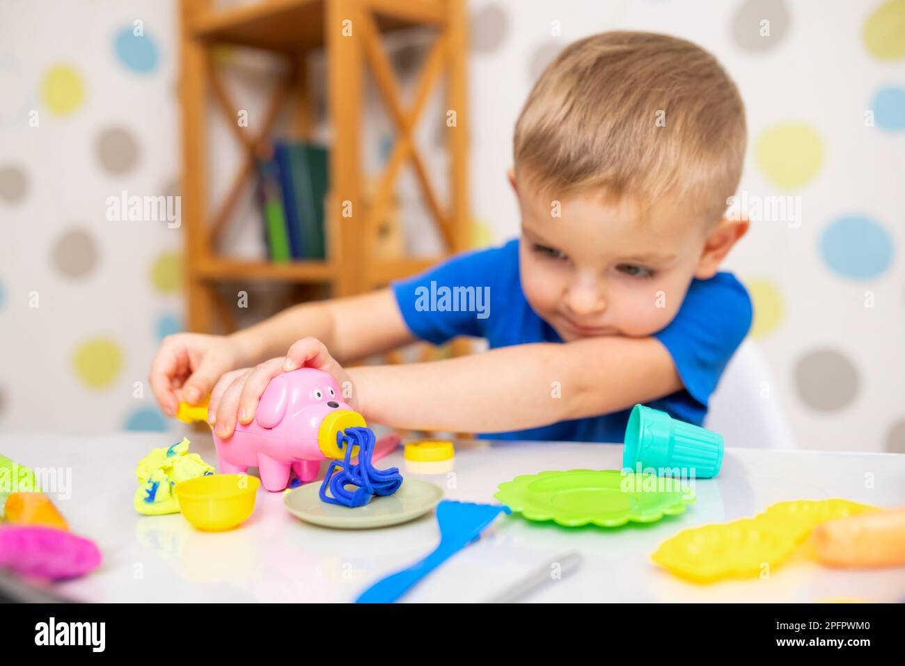 Cute child sitting at the table and plays with playdough Stock Photo ...