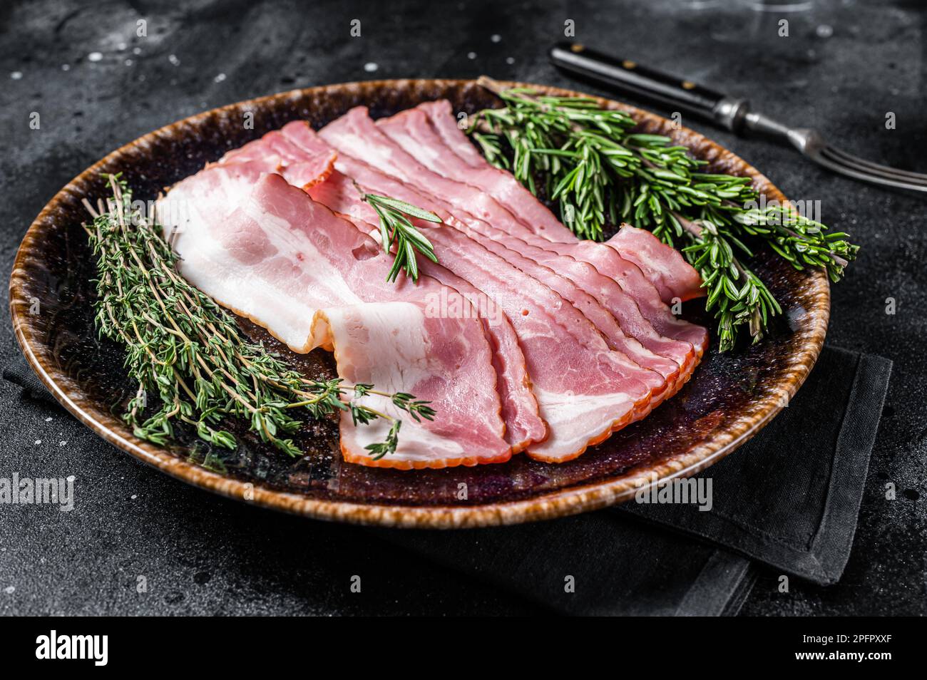 Raw sliced bacon ready for cooking with herbs. Black background. Top ...