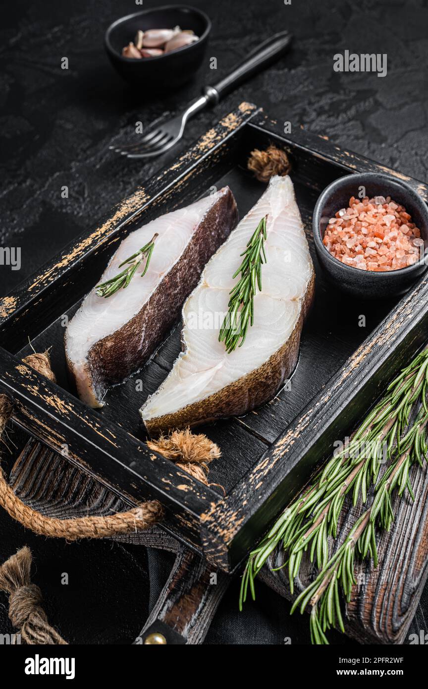 Raw halibut fish steak in wooden tray with herbs. Black background. Top ...