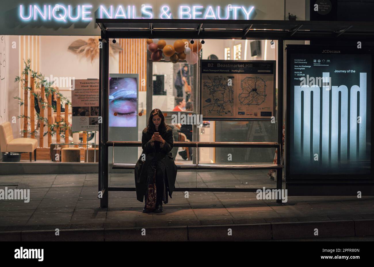 A woman waiting at the bus stop outside the nail salon Stock Photo - Alamy