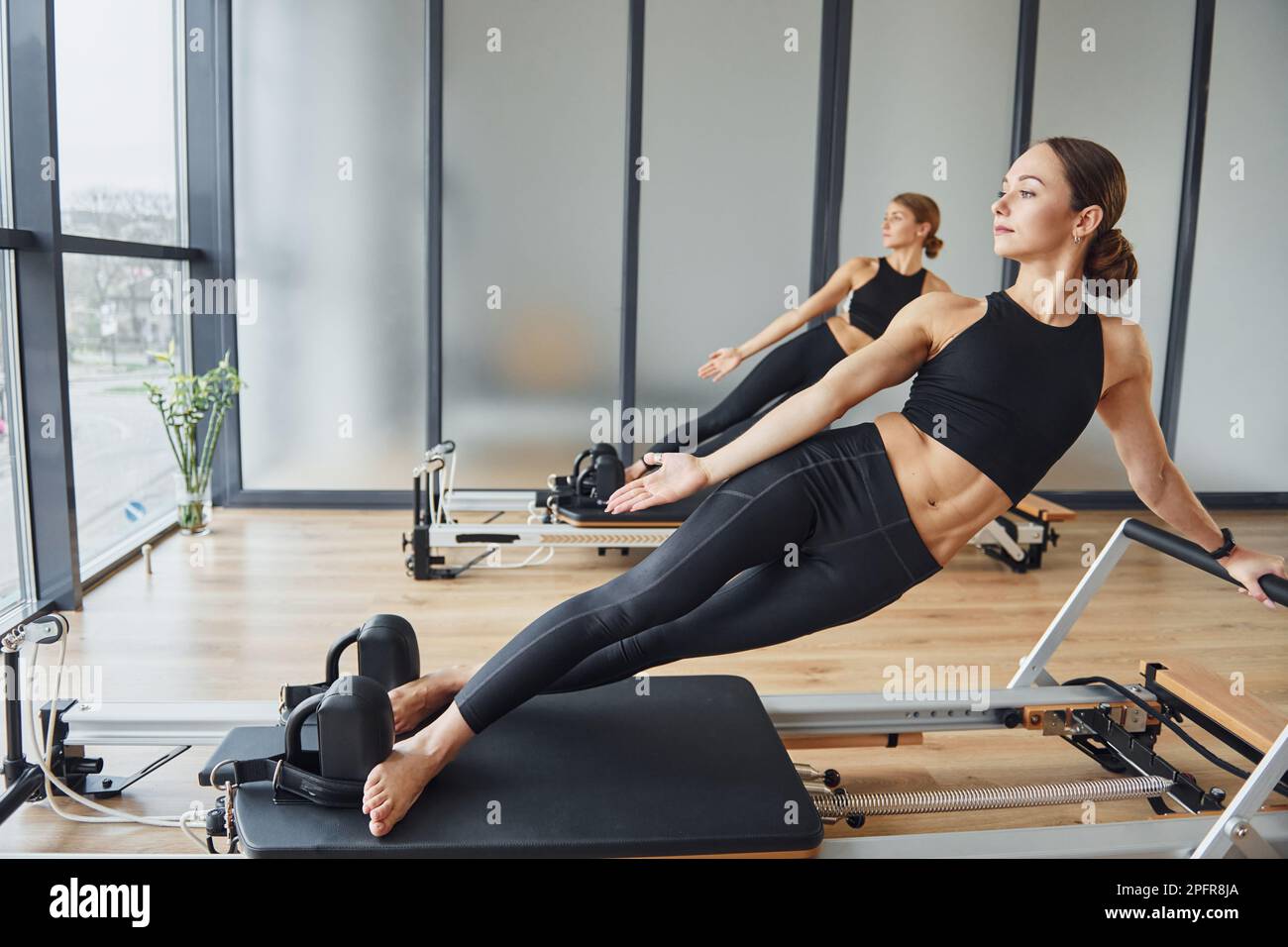 Standing on gym equipment and doing stretches. Two women in sportive wear and with slim bodies ...