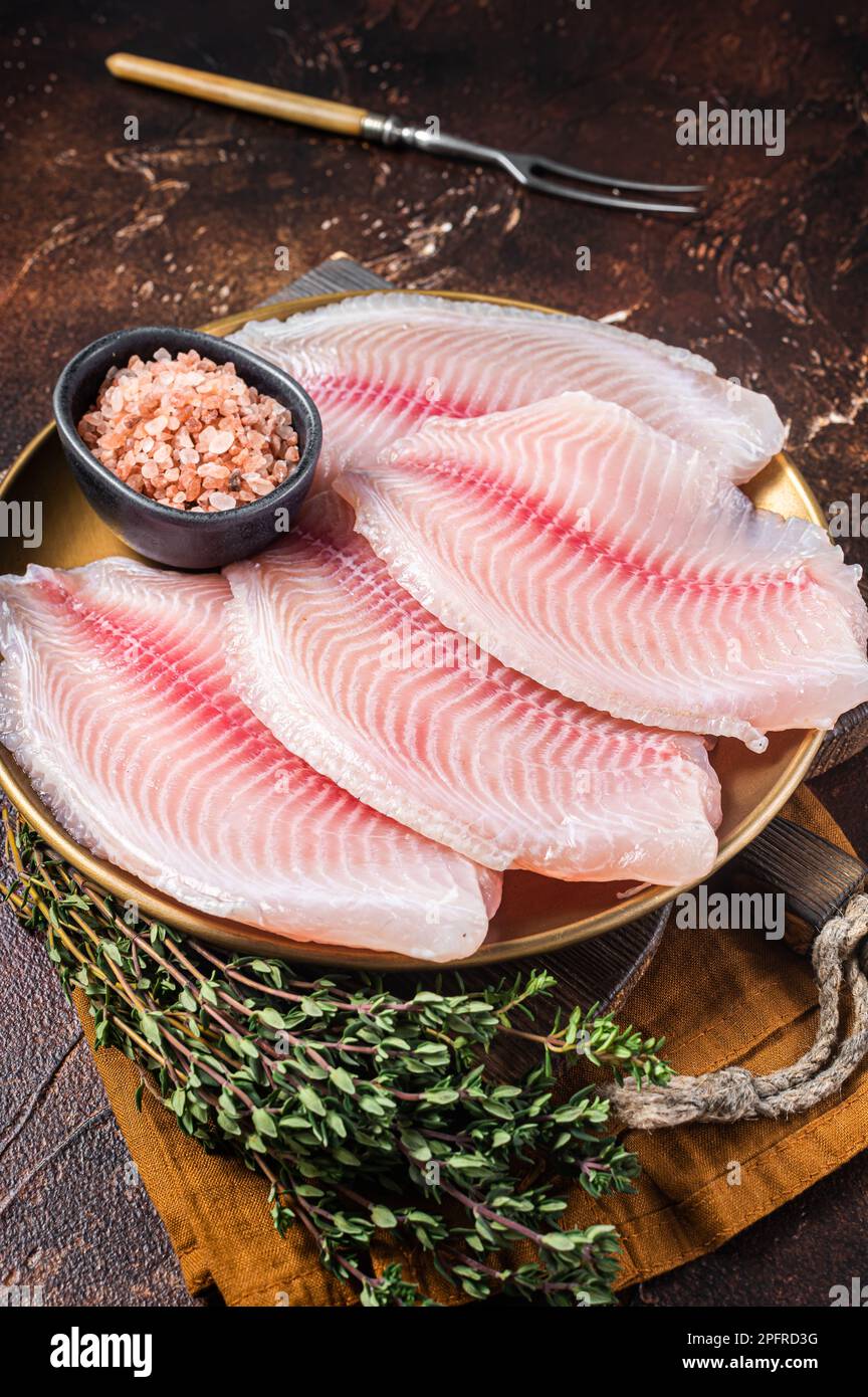 Raw fish fillet of tilapia in a plate with spices. Dark background. Top ...