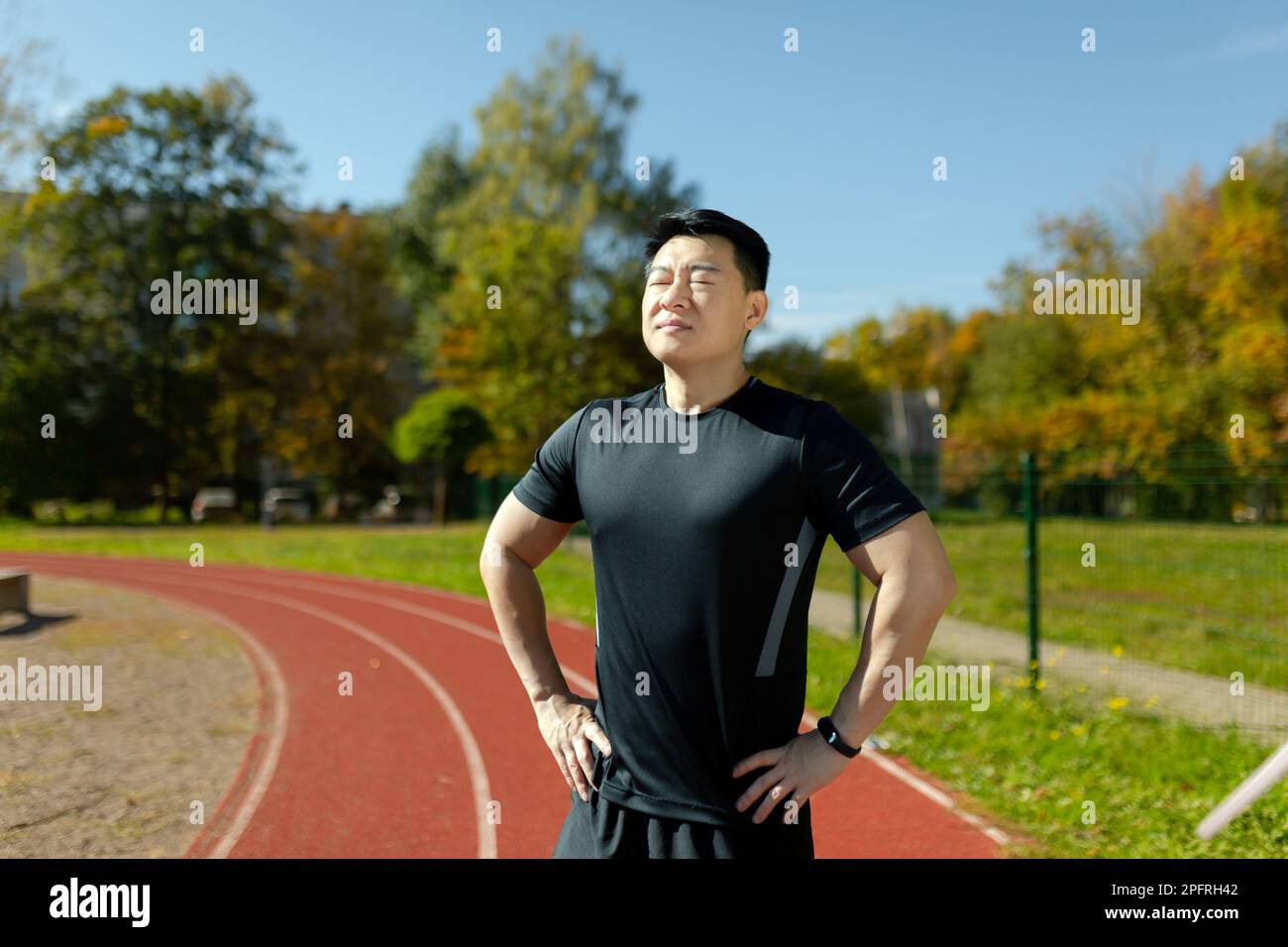 Portrait of a young Asian male athlete, trainer standing on a stadium ...