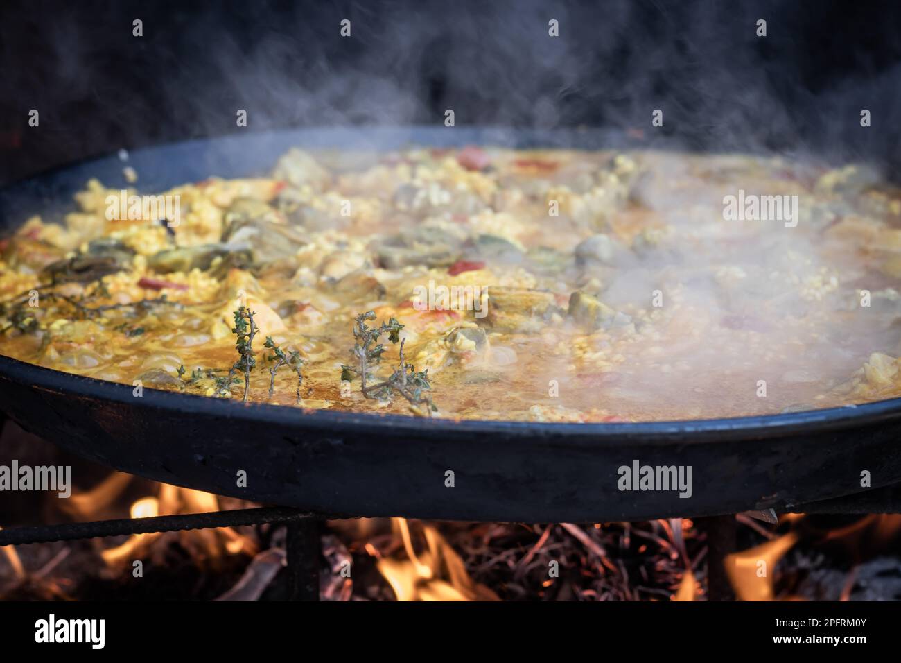 A large paella cooking over fire with a smokey background Stock Photo ...