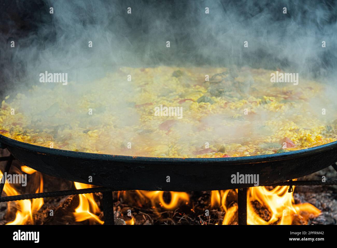 A large paella cooking over fire with a smokey background Stock Photo ...