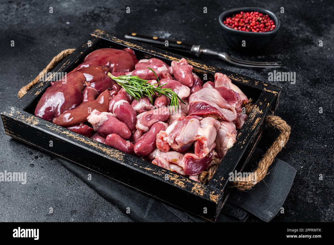 Uncooked Bird offals, raw chicken giblets, gizzards, stomachs, liver and hearts in a wooden tray ...