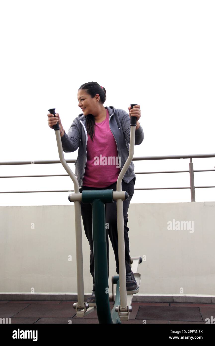 Adult 40-year-old Latina woman exercises on the roof garden of her apartment with shared public ...