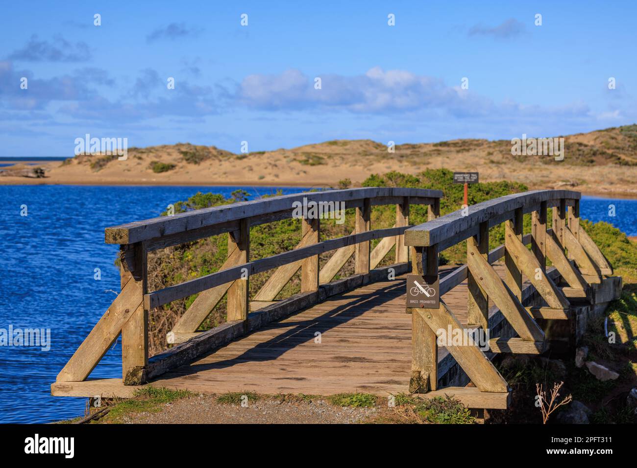 Wooden foot bridge with no cycling sign over blue water by dry sand ...