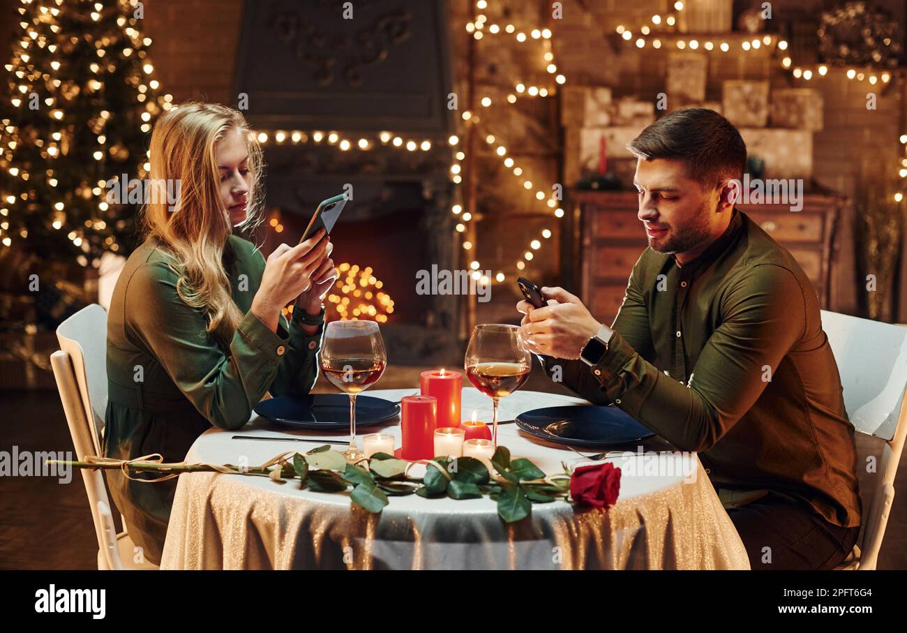 Sits and using phone. Young lovely couple have romantic dinner indoors ...