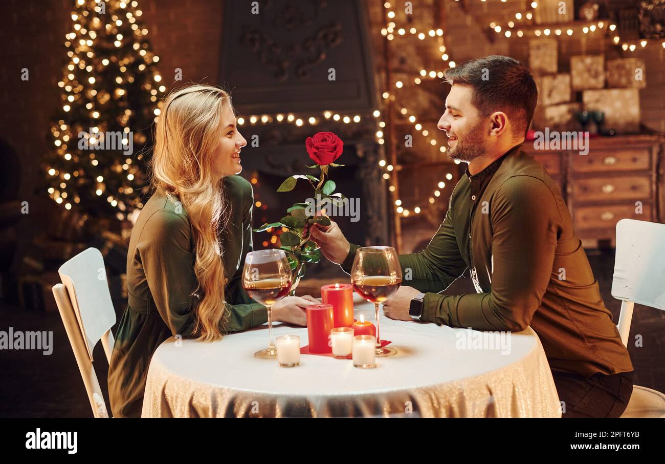 Holding beautiful red rose. Young lovely couple have romantic dinner ...