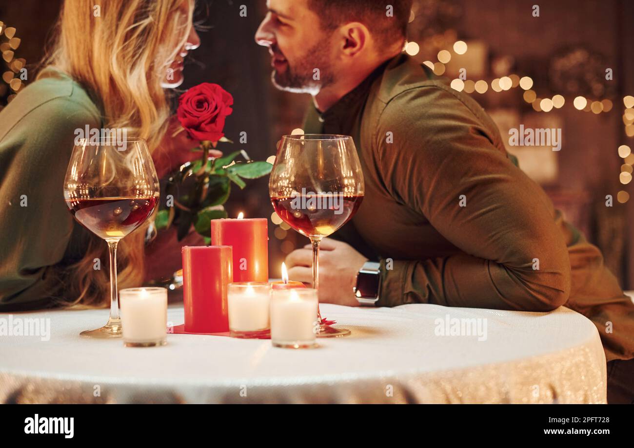 Holding beautiful red rose. Young lovely couple have romantic dinner ...