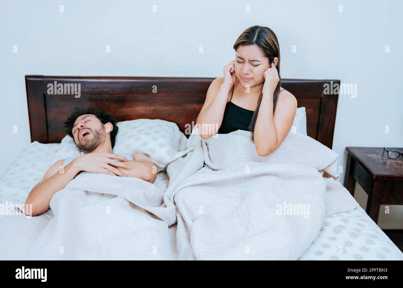 Husband snoring while the wife suffers and covers her ears. Sleep apnea concept, Snoring man in ...