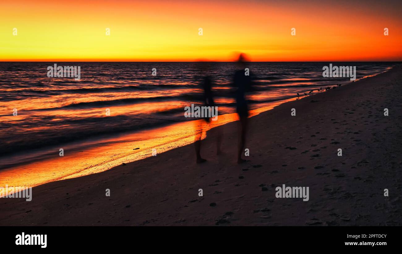 People walking on beach shore shadowed by sun rays Stock Photo - Alamy