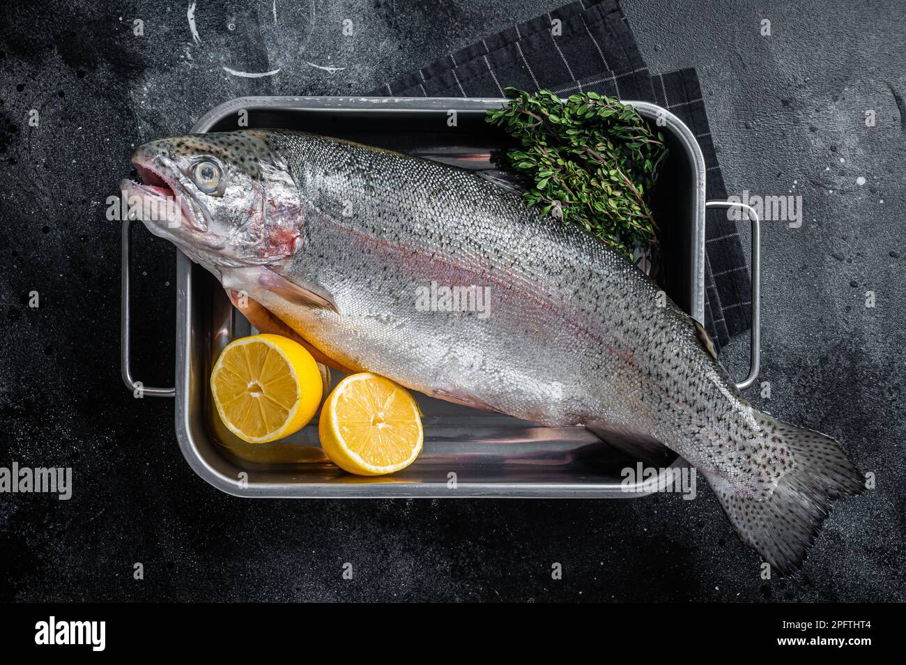 Raw whole trout fish in a kitchen tray with herbs. Black background ...