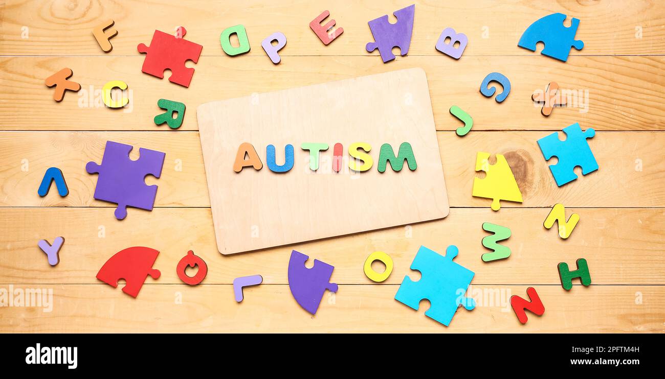 Word AUTISM, letters and puzzle pieces on wooden background Stock Photo ...