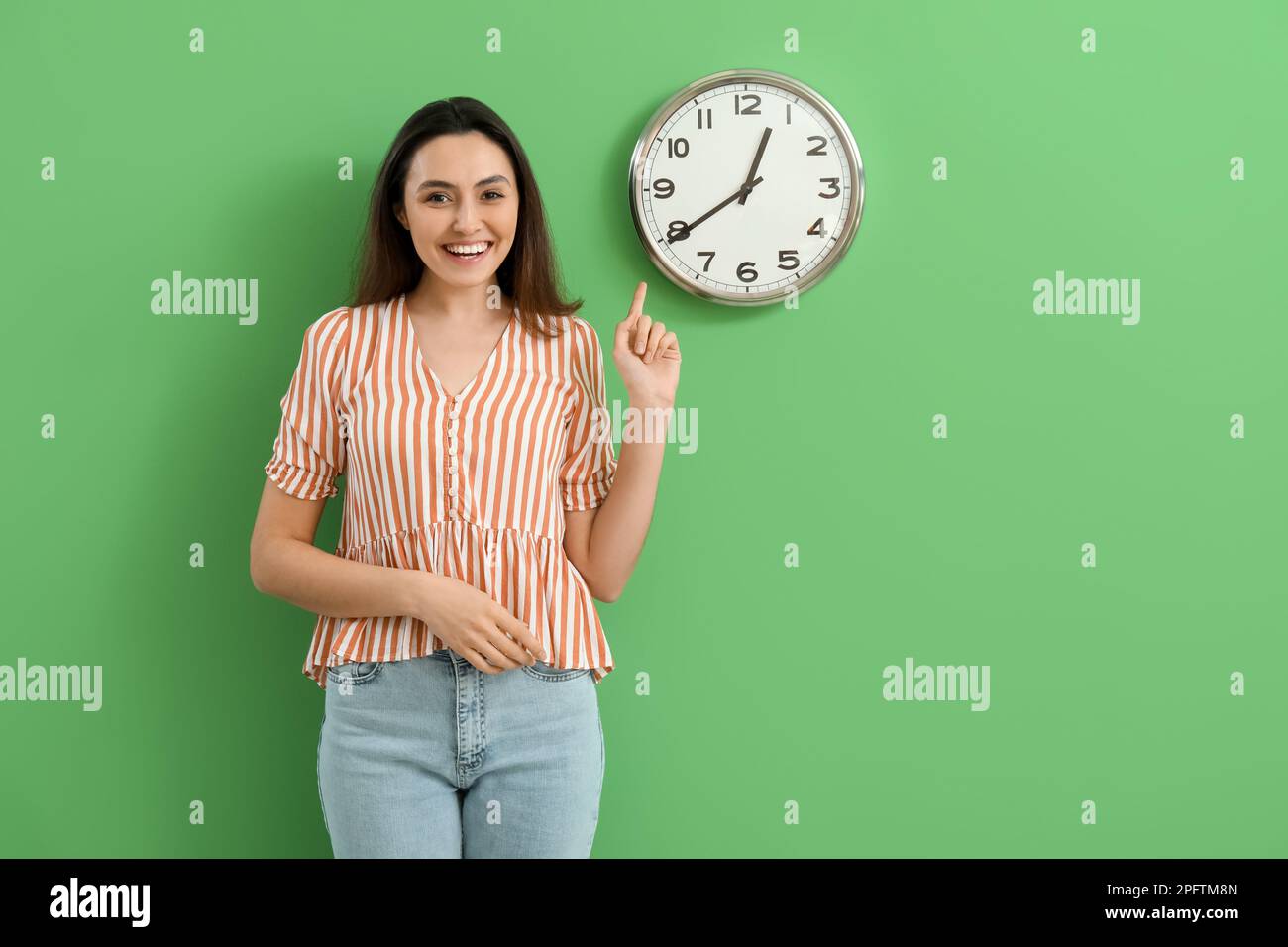 Young woman pointing at clock on green wall Stock Photo - Alamy