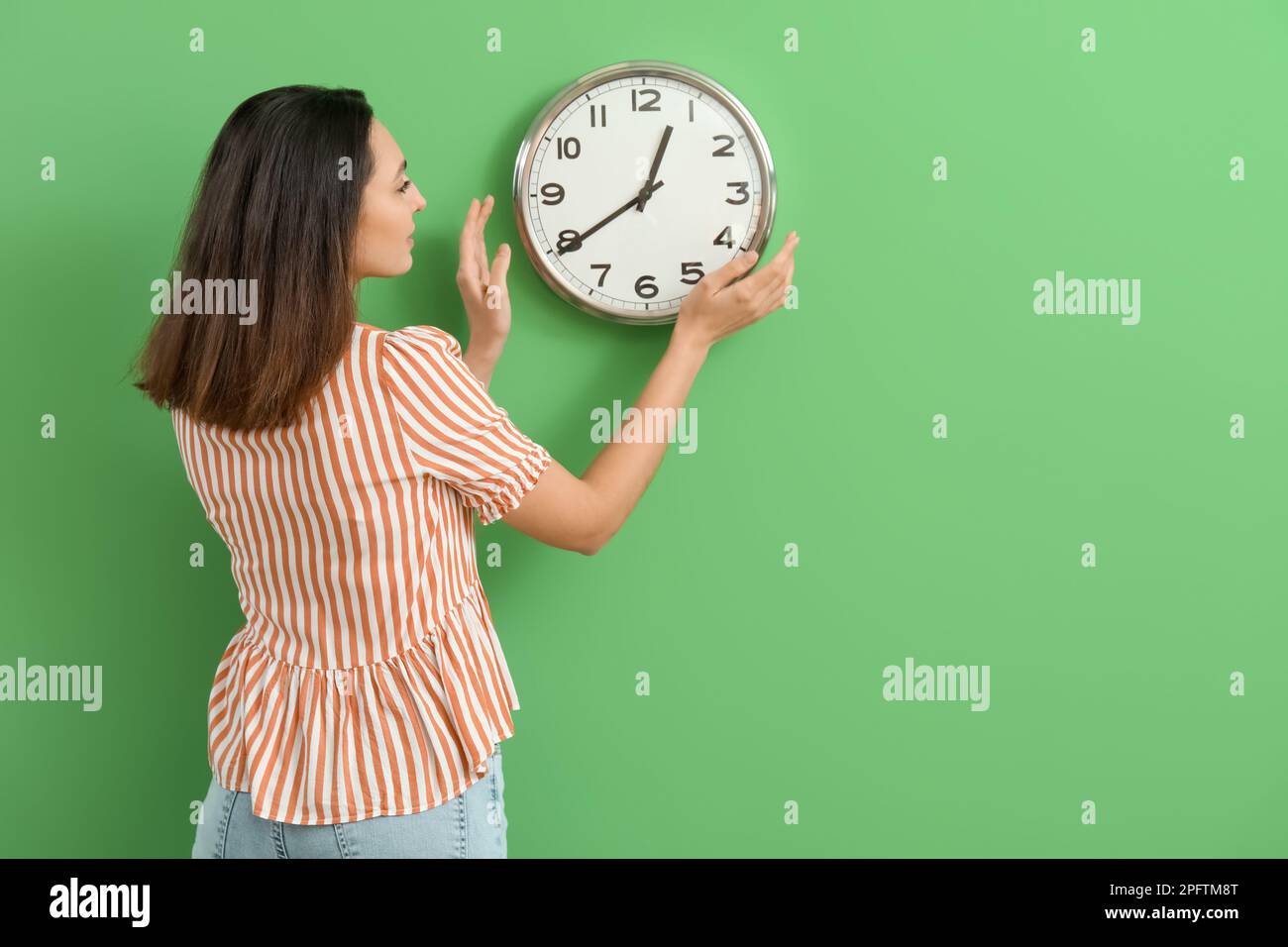 Young woman hanging clock on green wall, back view Stock Photo - Alamy