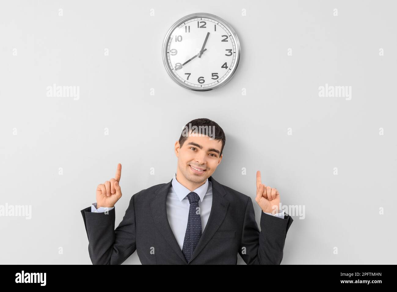 Young businessman pointing at clock on light wall Stock Photo - Alamy