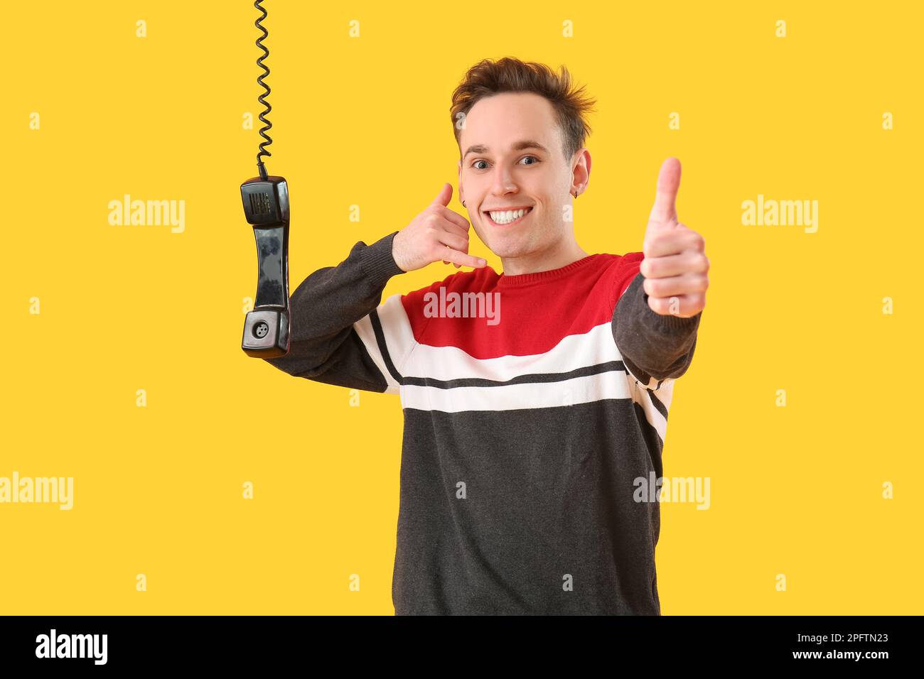 Cool young man showing "call me" and thumb-up gesture on yellow ...