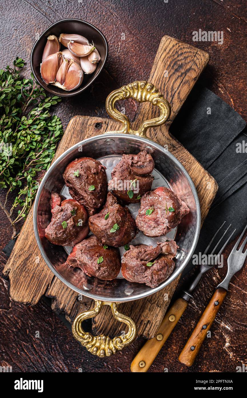 Roasted beef kidney, offal meat in skillet with herbs. Dark background ...