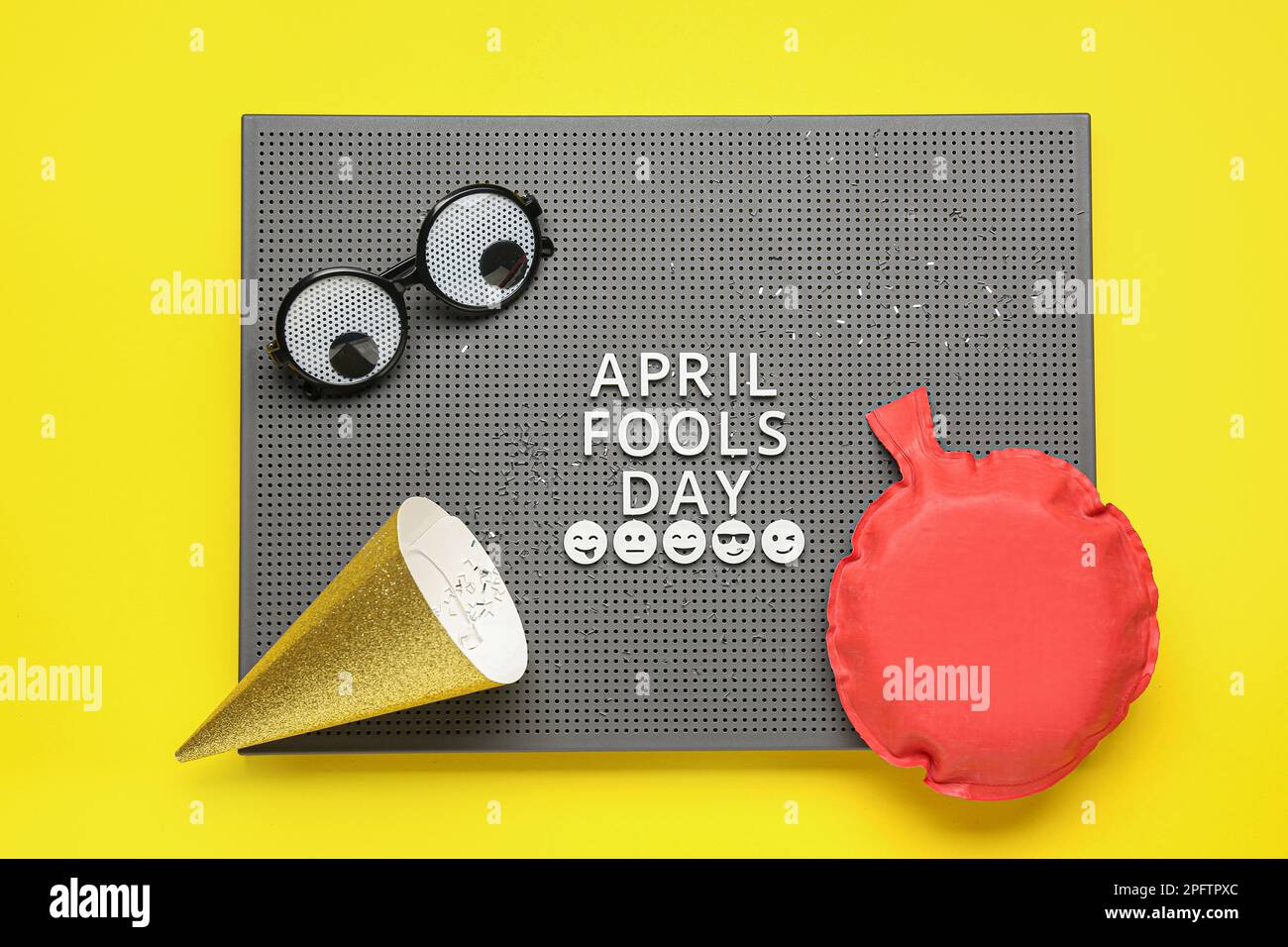 Board with text APRIL FOOLS DAY, funny decor and party hat on yellow ...