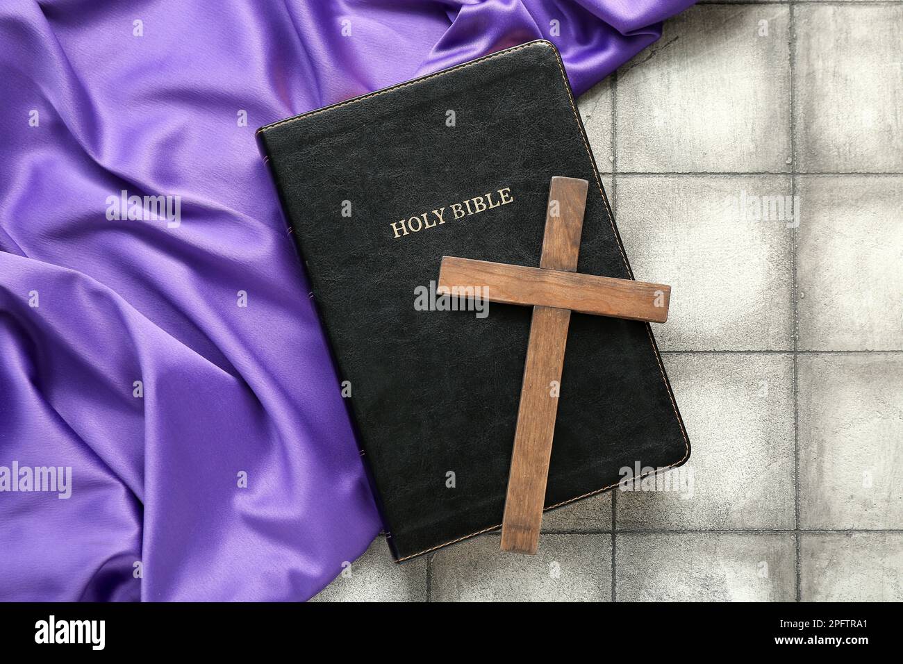 Holy Bible with wooden cross and purple fabric on grey tile background ...