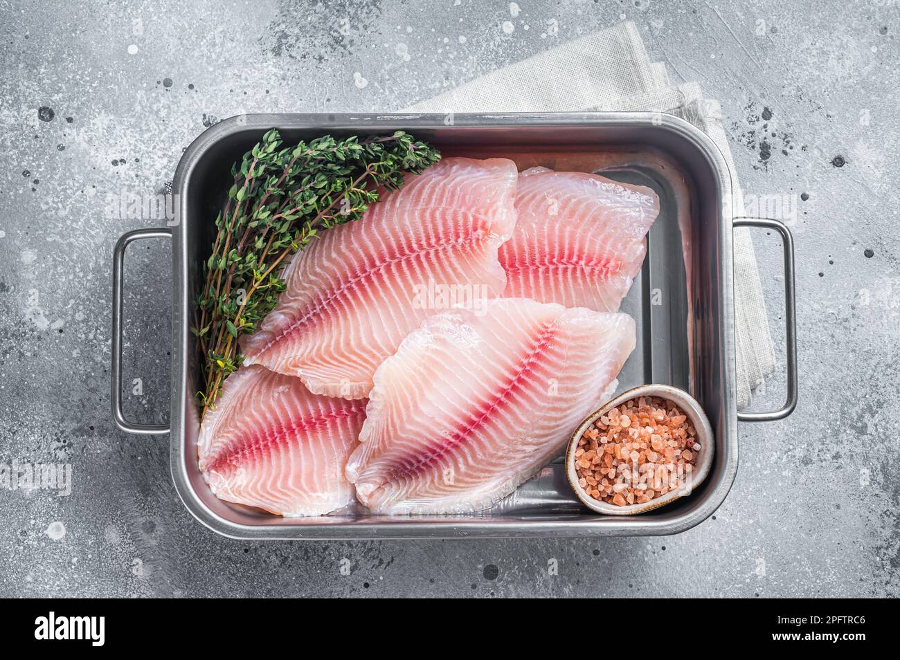 Raw white fish tilapia, uncooked fillet in kitchen tray with herbs ...