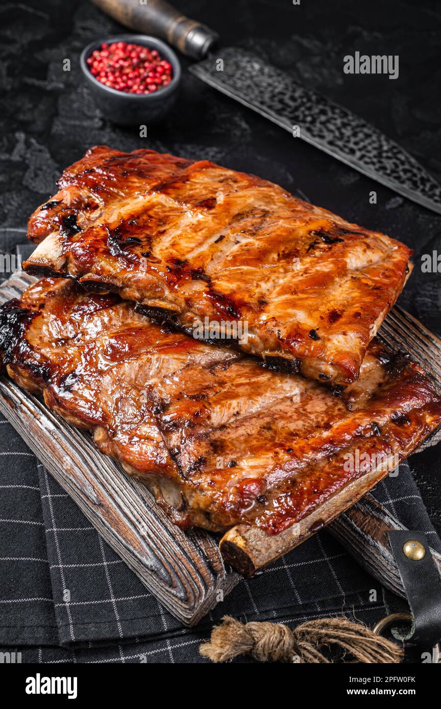 Stack of grilled pork ribs in BBQ sauce on a chopping board. Black ...