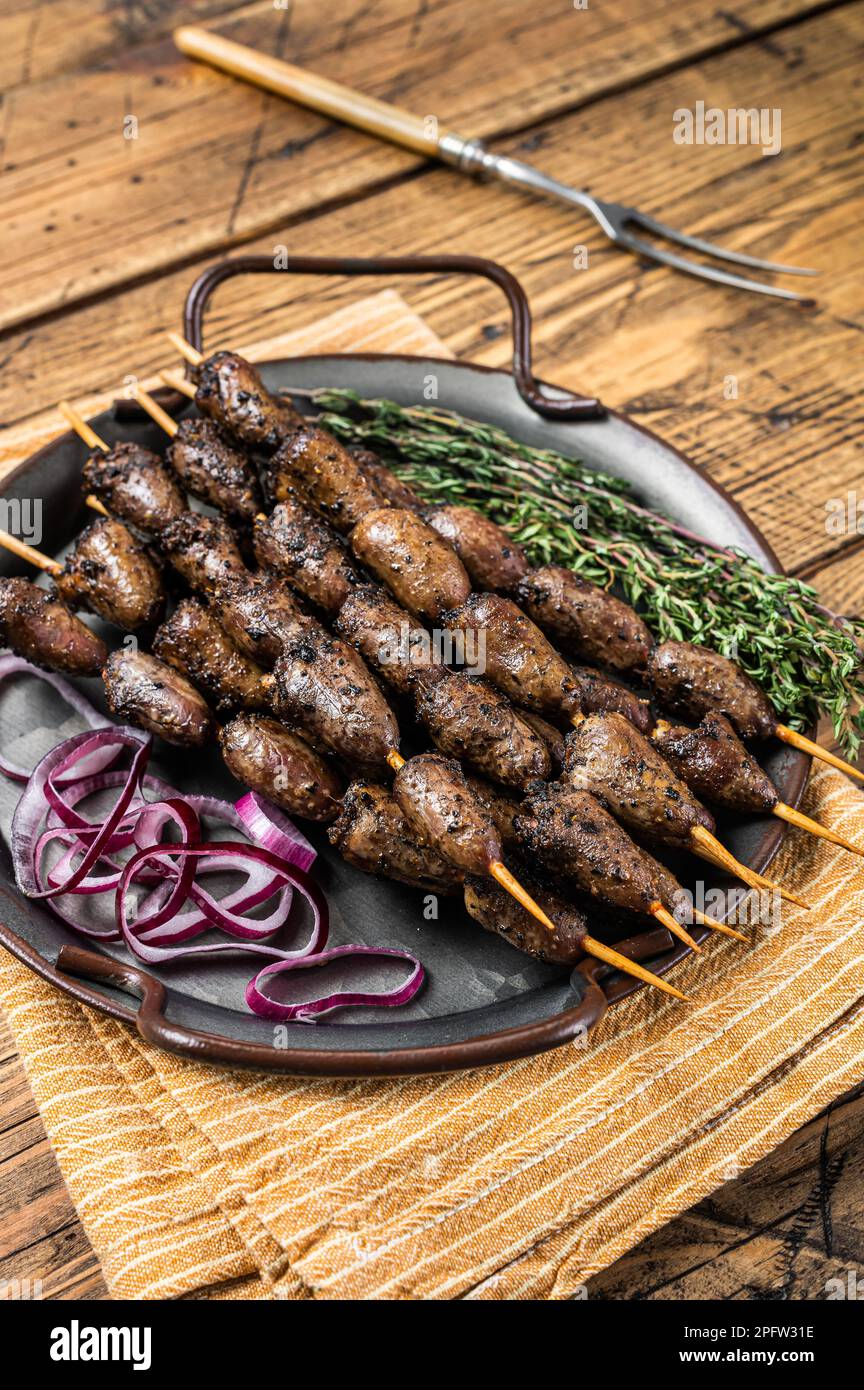 Churrasco Brazilian barbecue, chicken hearts grilled kebabs with herbs and vegetables. Wooden ...