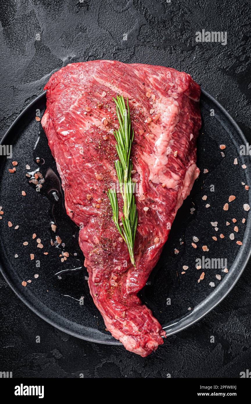 Seasoned raw tri-tip beef meat steak on plate. Black background. Top ...