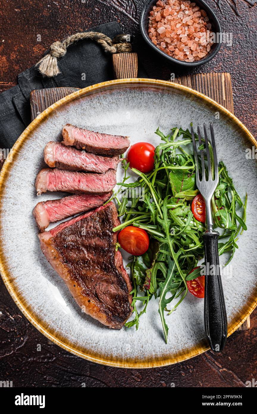 Grilled Top sirloin beef meat steak in plate with vegetable salad. Dark ...