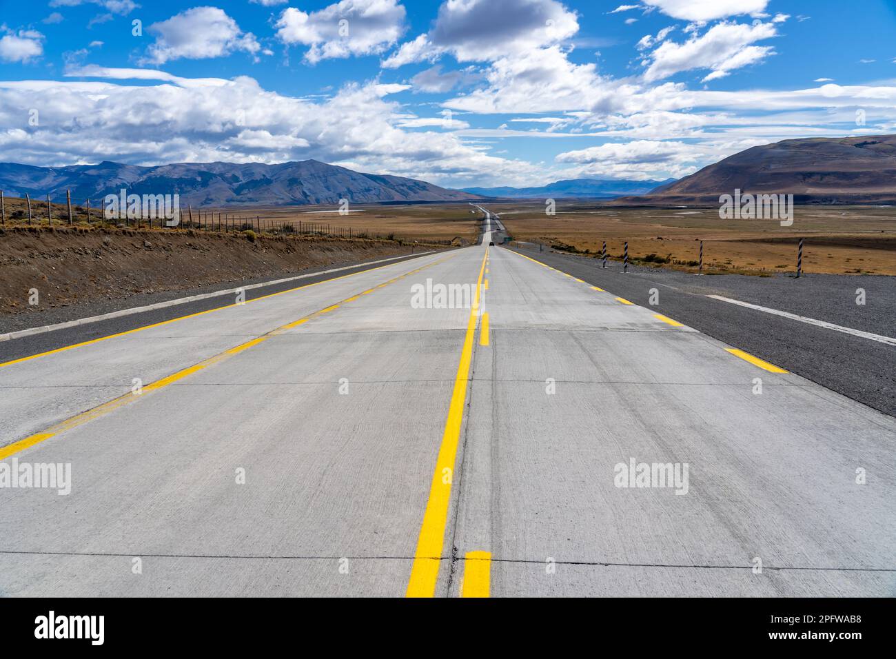 A long straight road with yellow lines leading towards mountains that ...