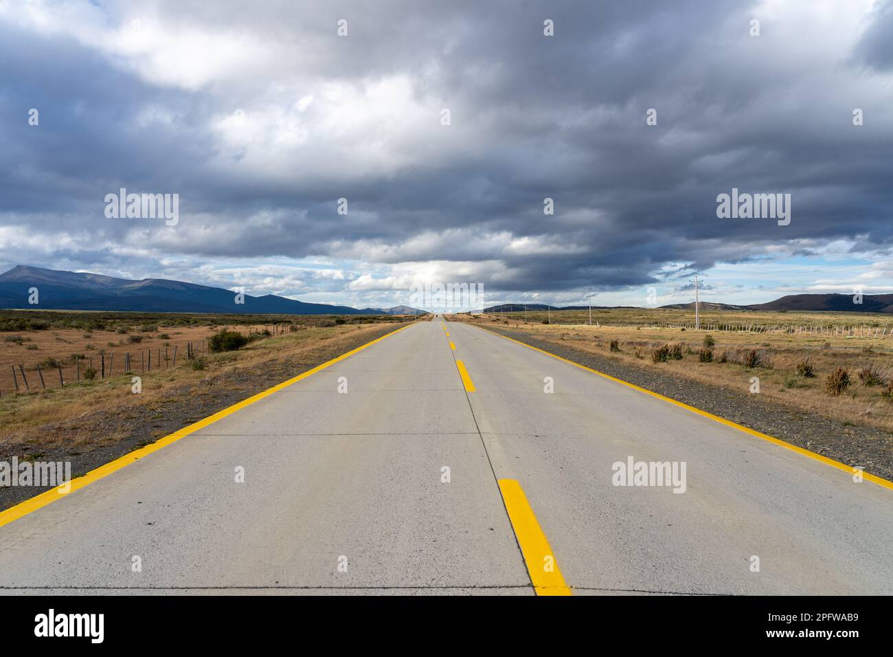 A long straight road with yellow lines leading towards mountains that ...