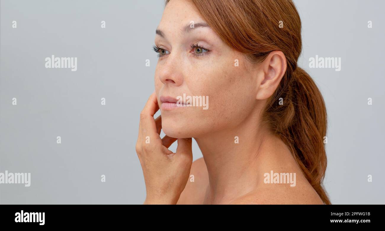 Portrait of middle aged woman with reddish hair holding hand on cheek ...