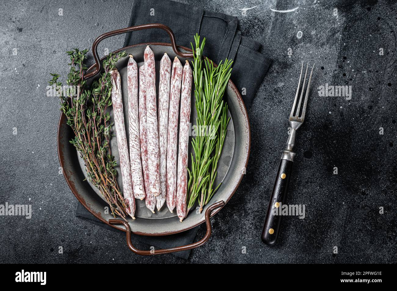 Spanish tapa mini fuet sausage with herbs. Black background. Top view ...