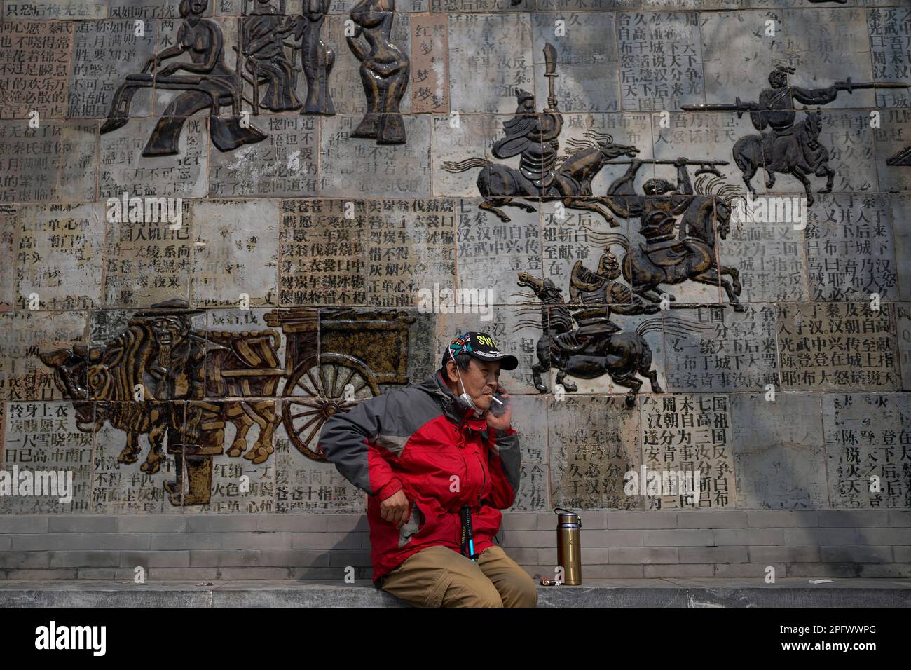 A man smokes as he rests near a wall depicting poems of Chinese history ...