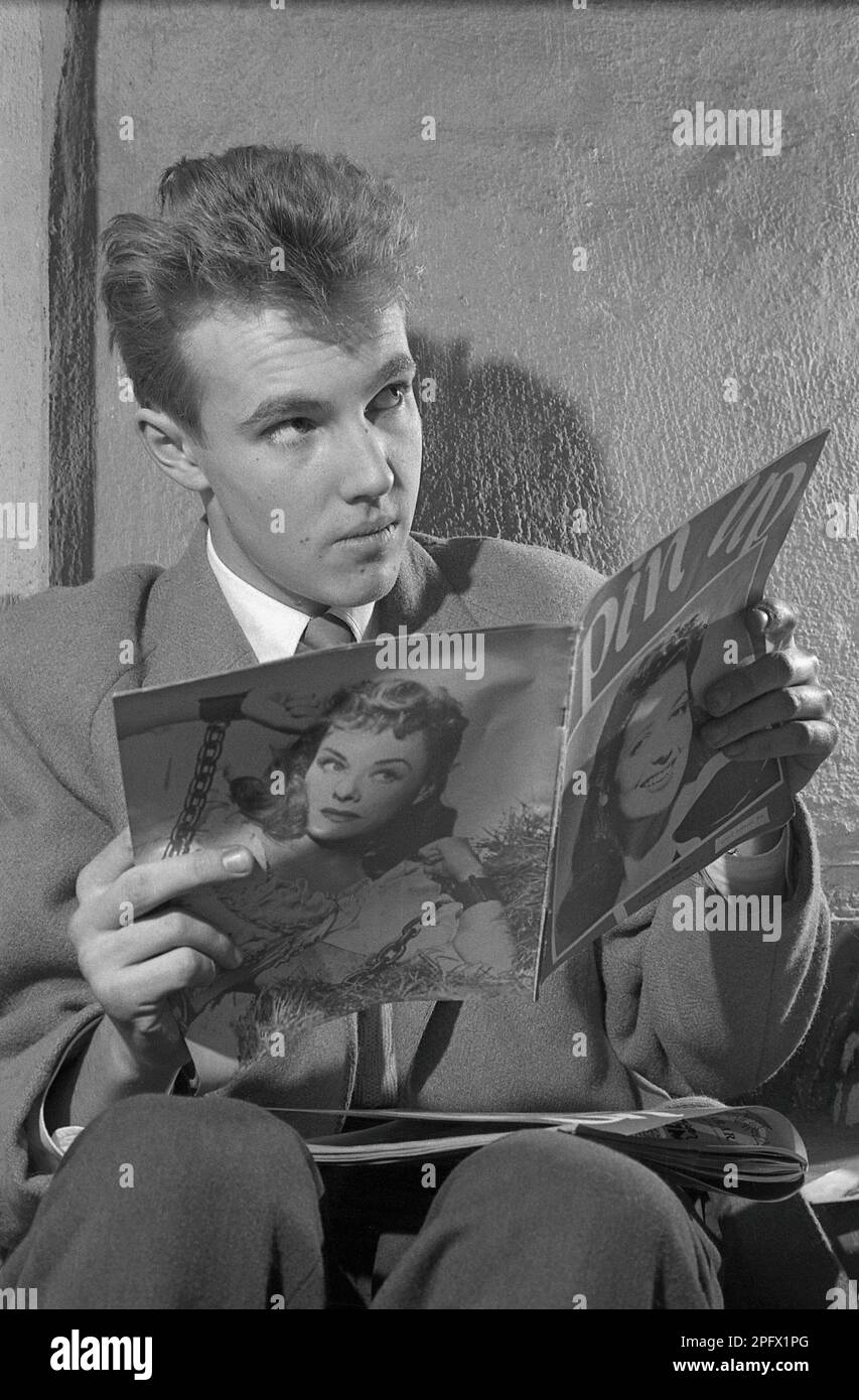 Reading a pin-up magazine in the 1950s. A young man looks secretive ...