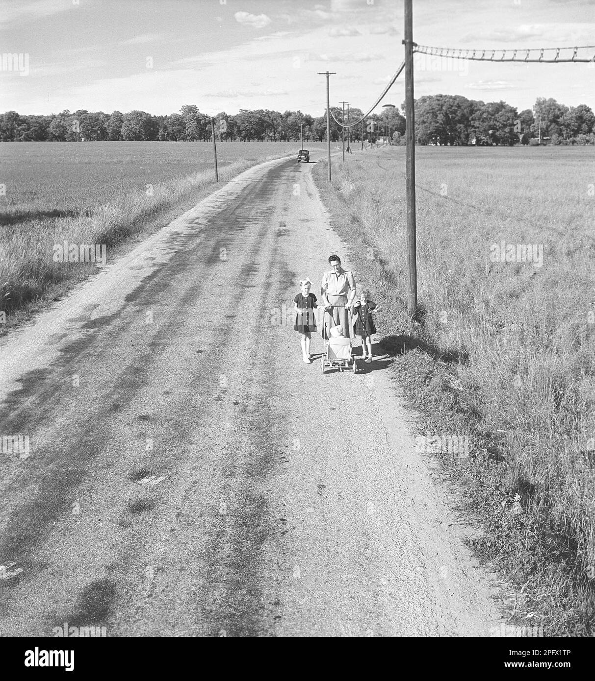 Parents in the 1940s. A mother and her daughters walk along a road with ...