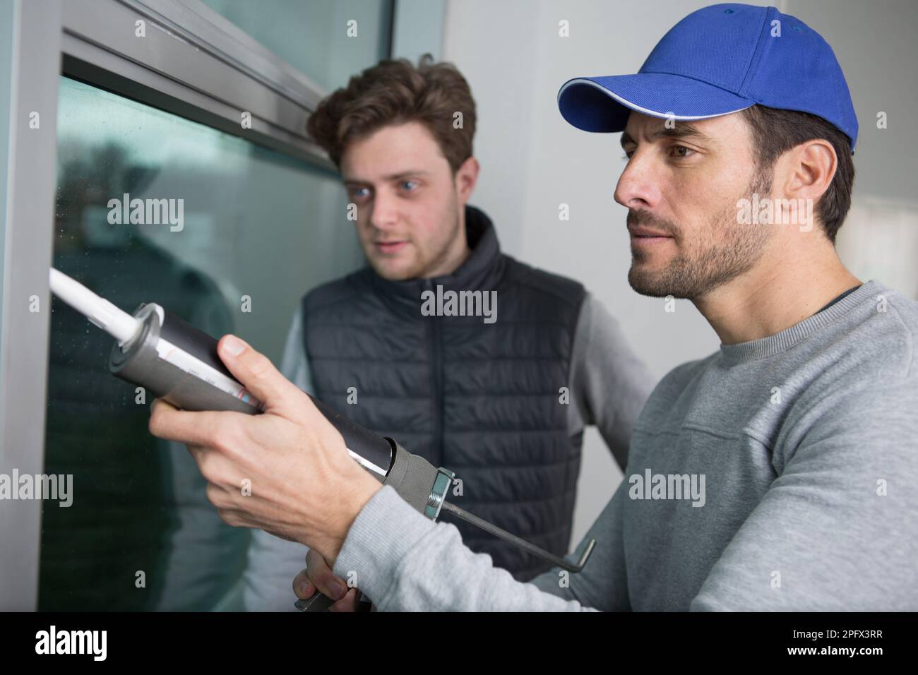 apprentice being shown how to apply caulk to window Stock Photo - Alamy