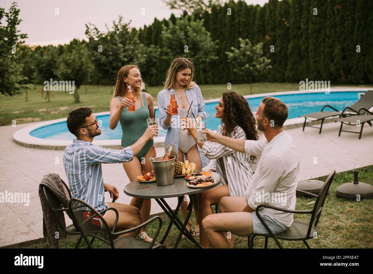 Group of happy young people cheering with cider by the pool in the ...