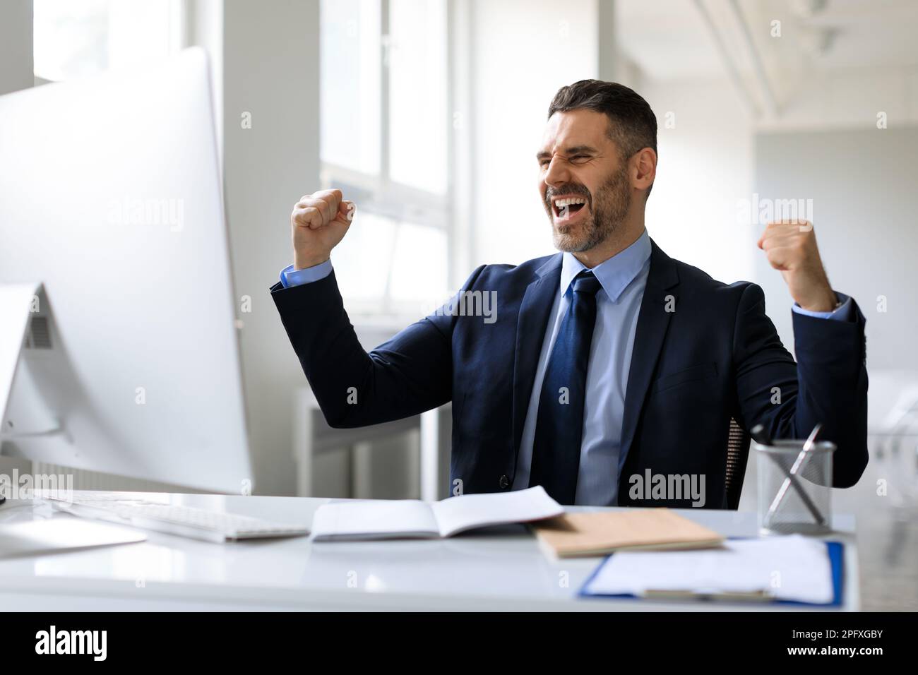 Happy businessman celebrating success with computer in office, looking ...