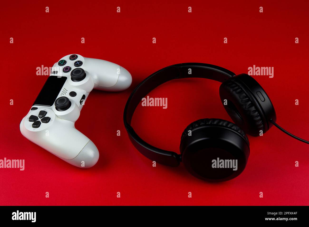 White video games controller and black headphones on a red table top ...