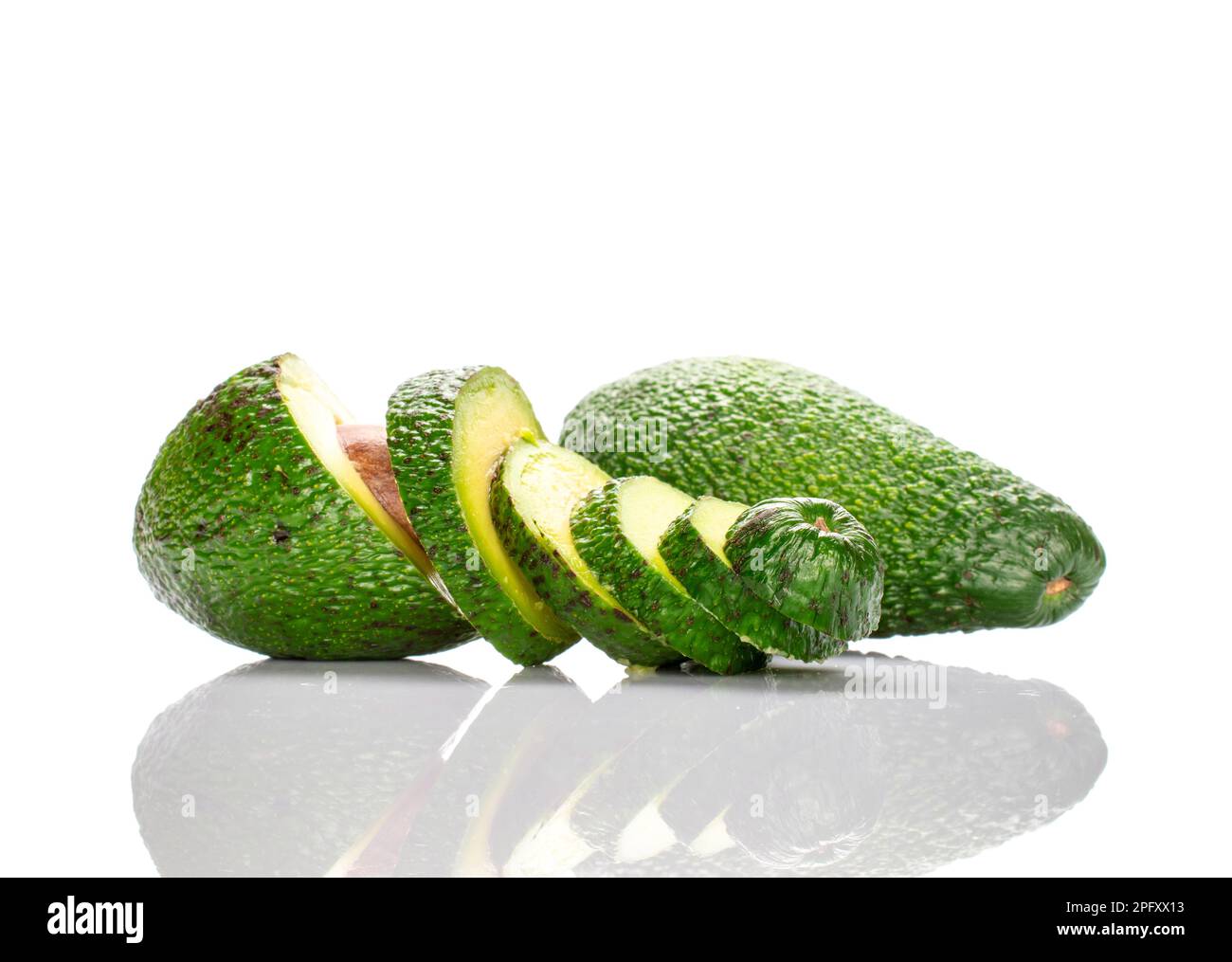 One whole green ripe avocado, the second avocado is cut into transverse ...