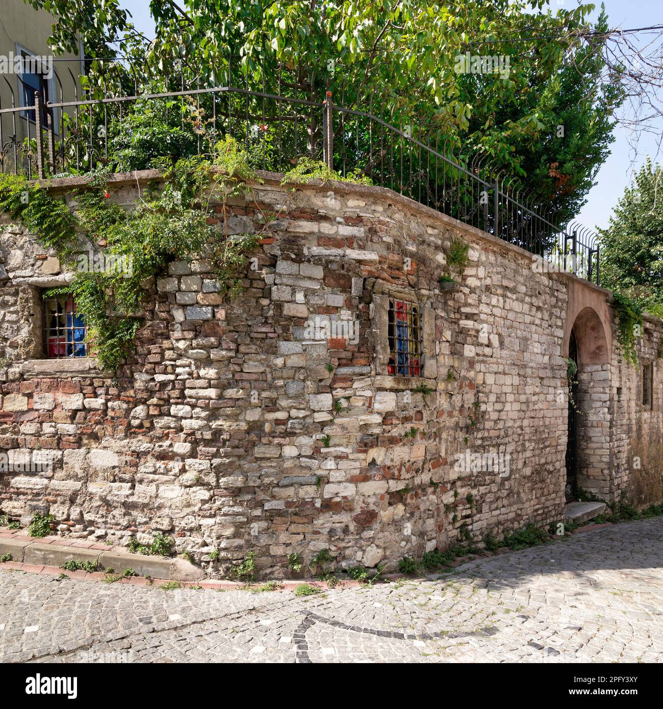 Old abandoned building, with weathered stone wall, and wrought iron windows, partially covered ...
