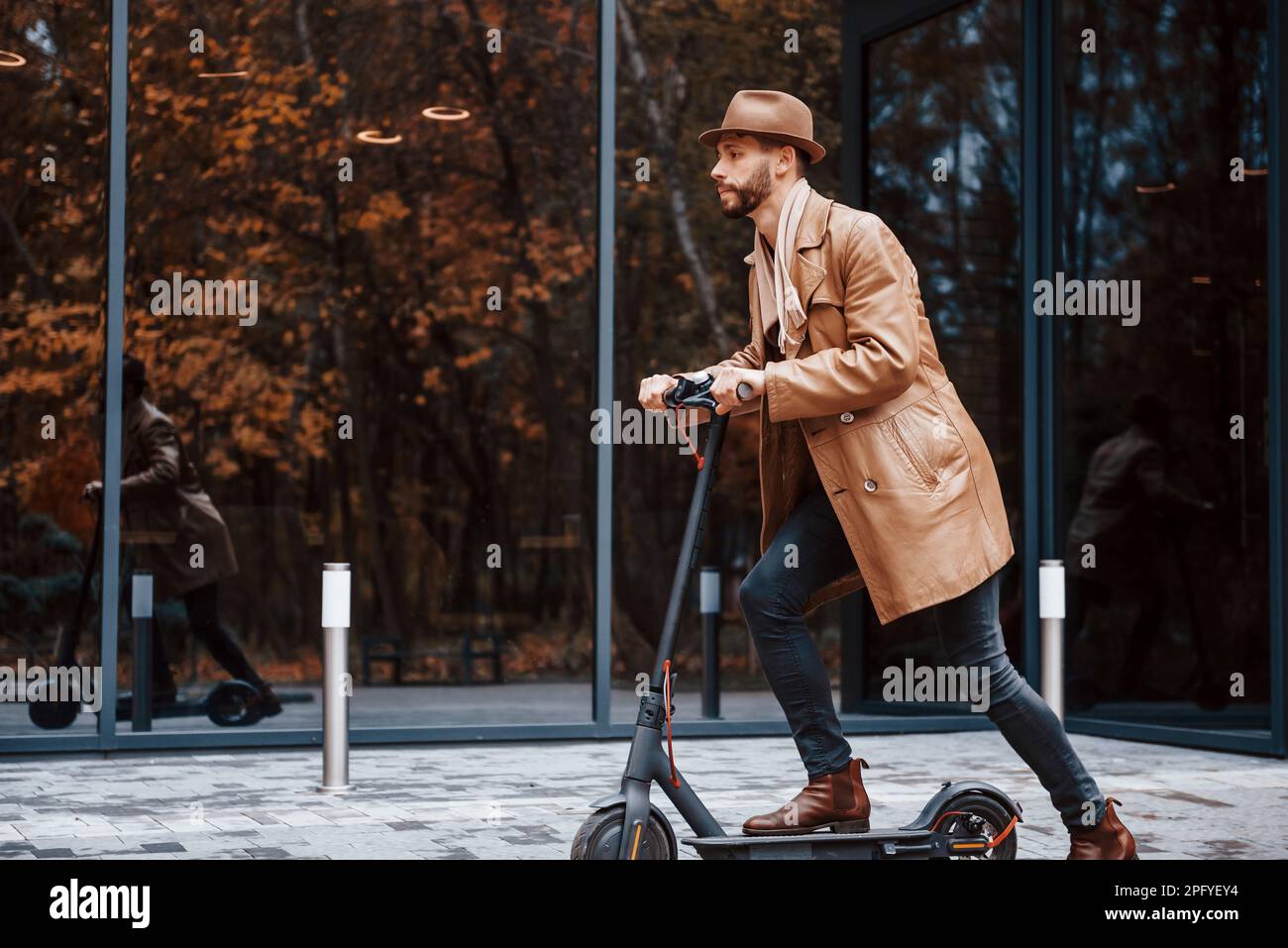 Riding electric scooter. Young male model in fashionable clothes is ...