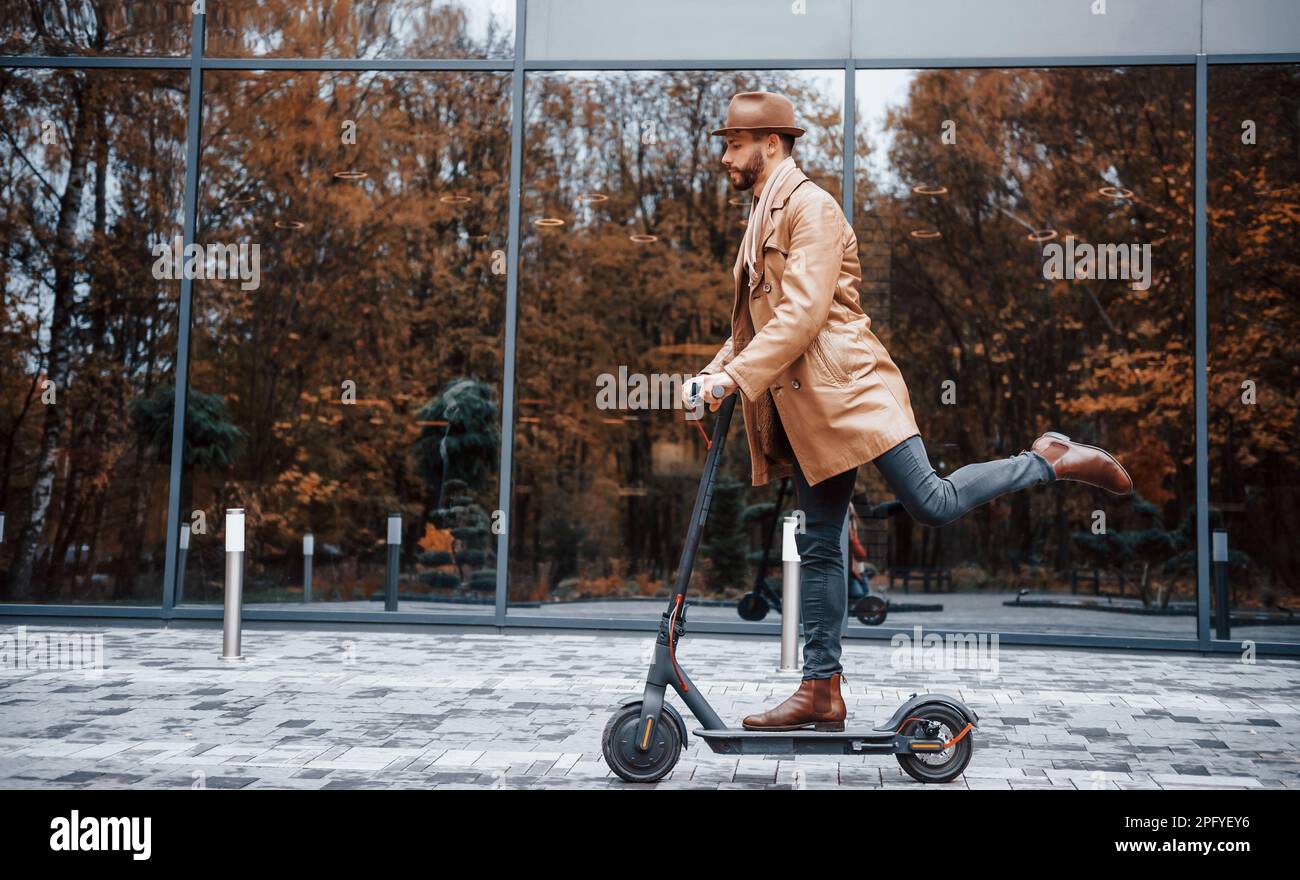 Riding electric scooter. Young male model in fashionable clothes is ...