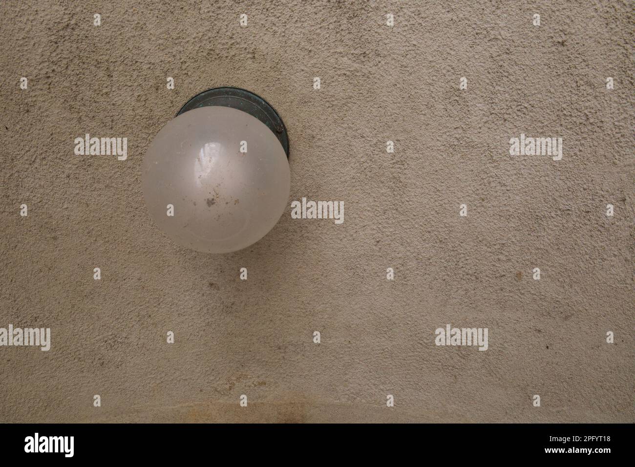 Old, exterior light with off-white, textured, plaster wall that appears ...