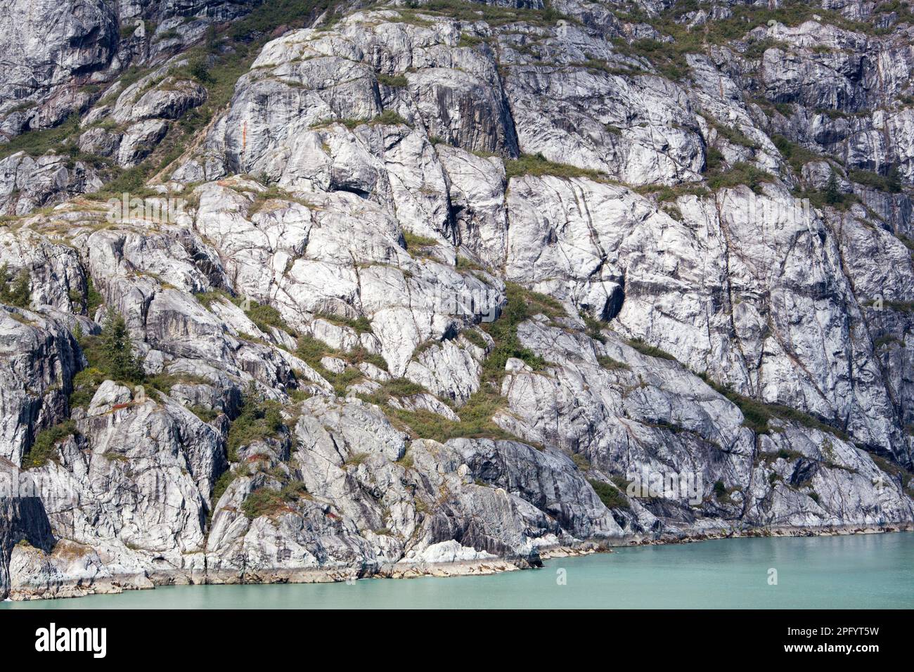 The steep rocky shore by turquoise color water in Glacier Bay national ...