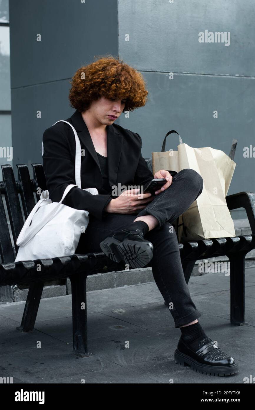 non-binary person is watching the smartphone sittig o a bench Stock ...