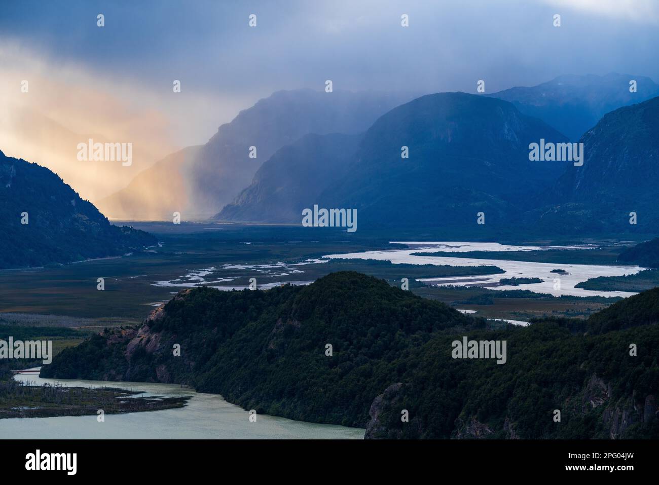 Rays of sunshine break through the rain clouds over the river valley of ...